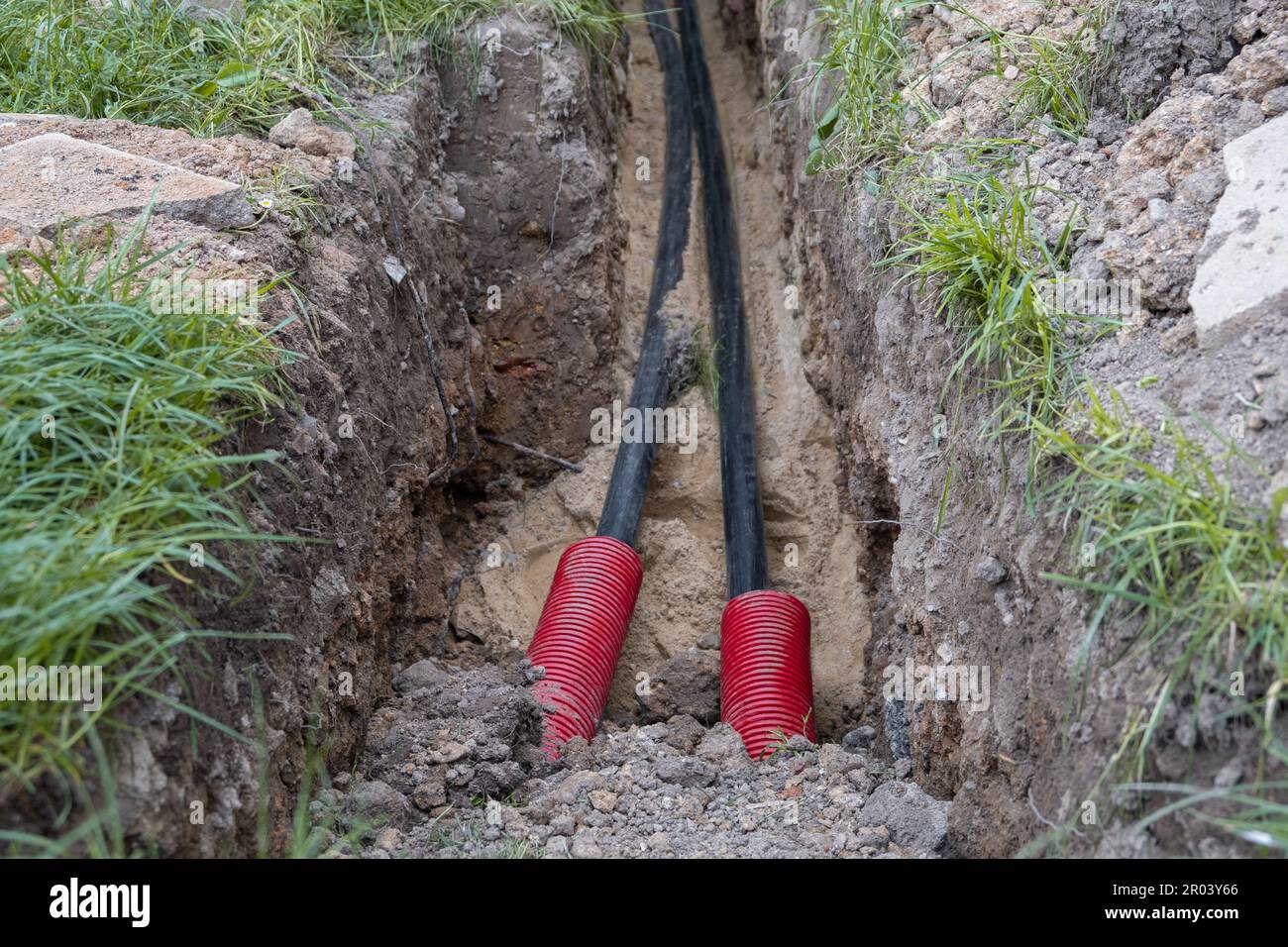 Electric cables in red corrugated pipe are buried underground on the ...