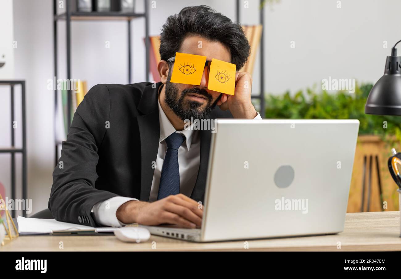 Inefficient tired young businessman working sleeping on laptop computer with eyes stickers on ...