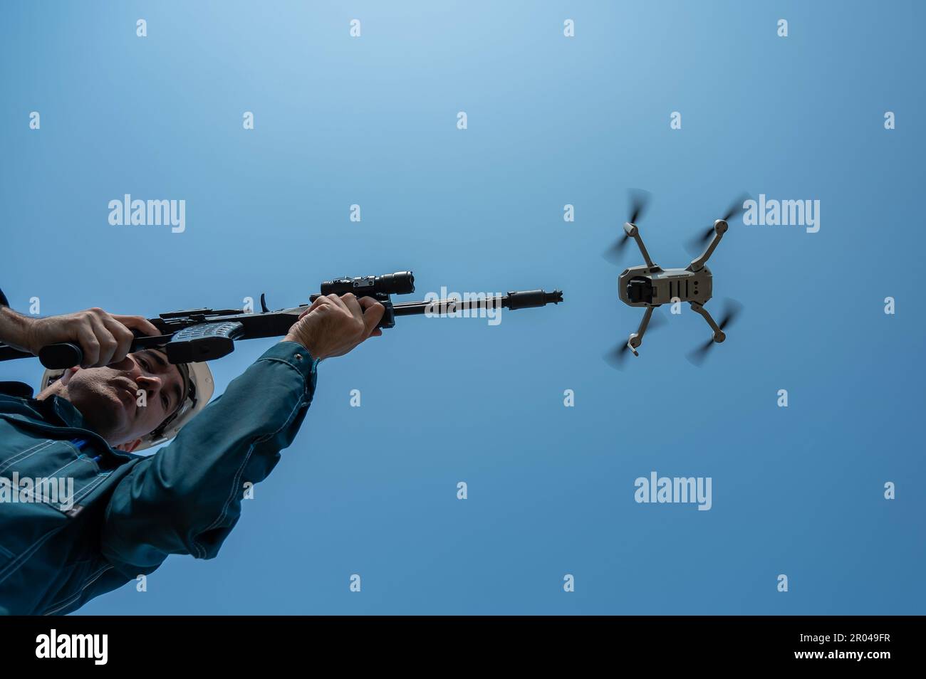 A man aims to shoot a rifle at a flying drone against a blue sky Stock ...
