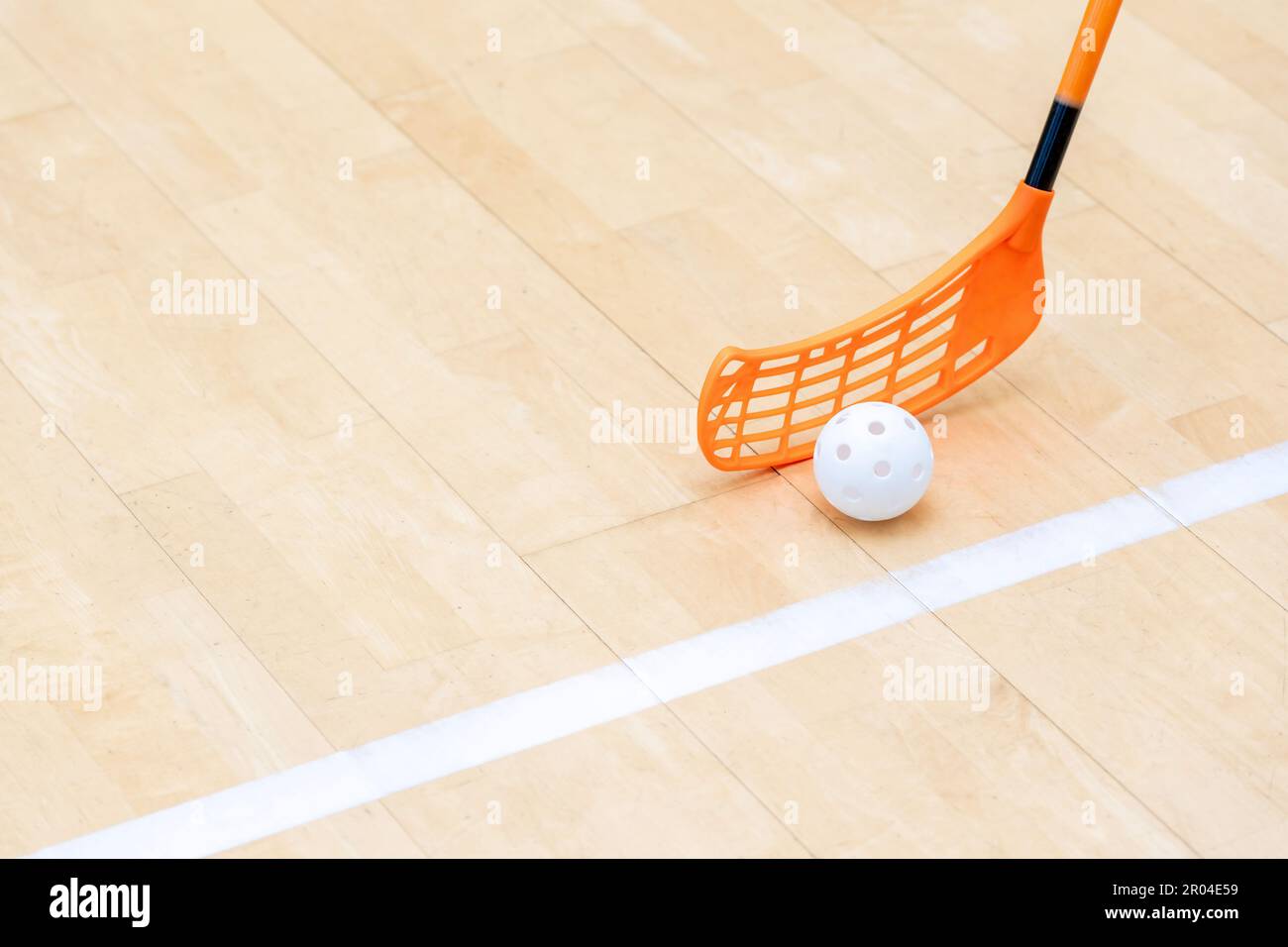 Floorball stick and white ball on hardwood court floor. Horizontal ...