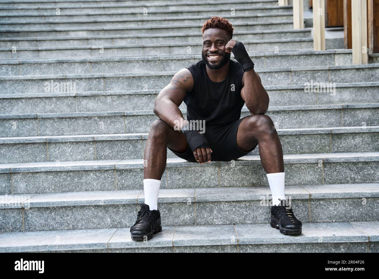 Fit happy sporty young black man boxer fighter sitting at urban stairs ...