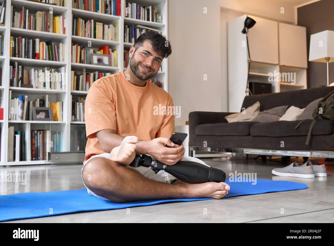 Happy man with prosthetic leg disability doing yoga using phone at home ...