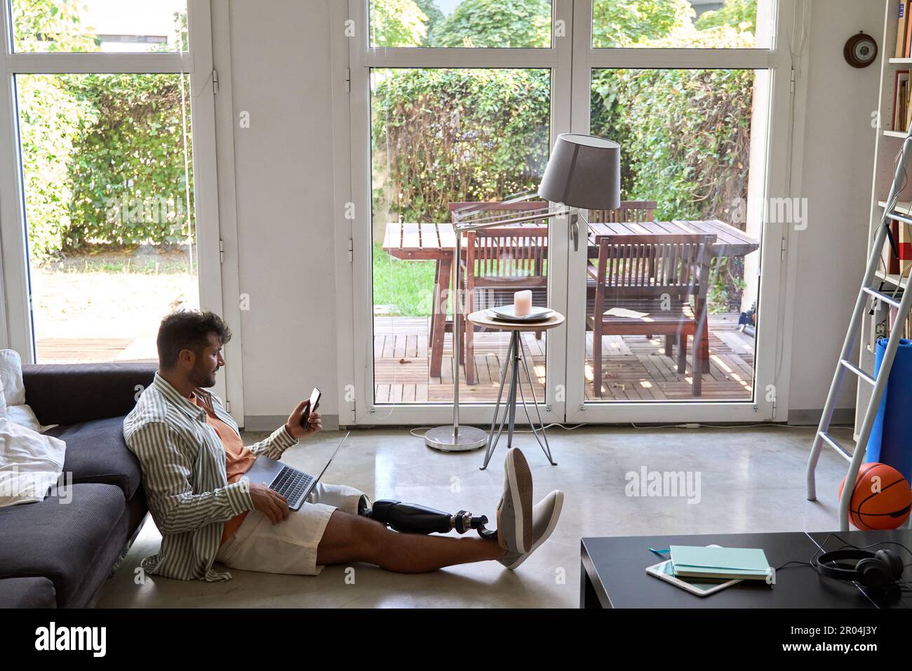 Man with disability leg prosthesis sitting home using phone and laptop ...