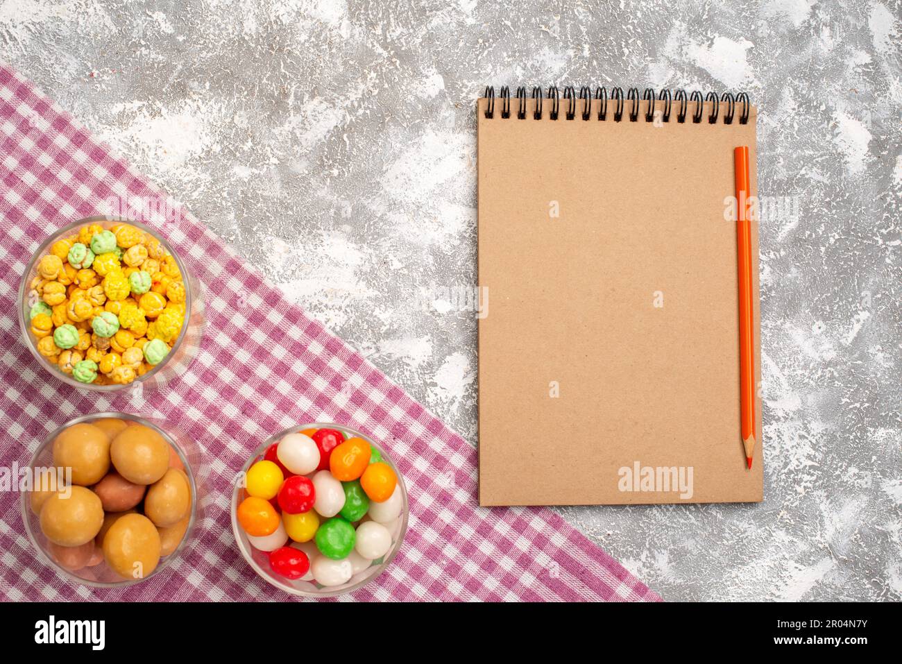 top view different sweet candies inside glasses with notepad on white ...
