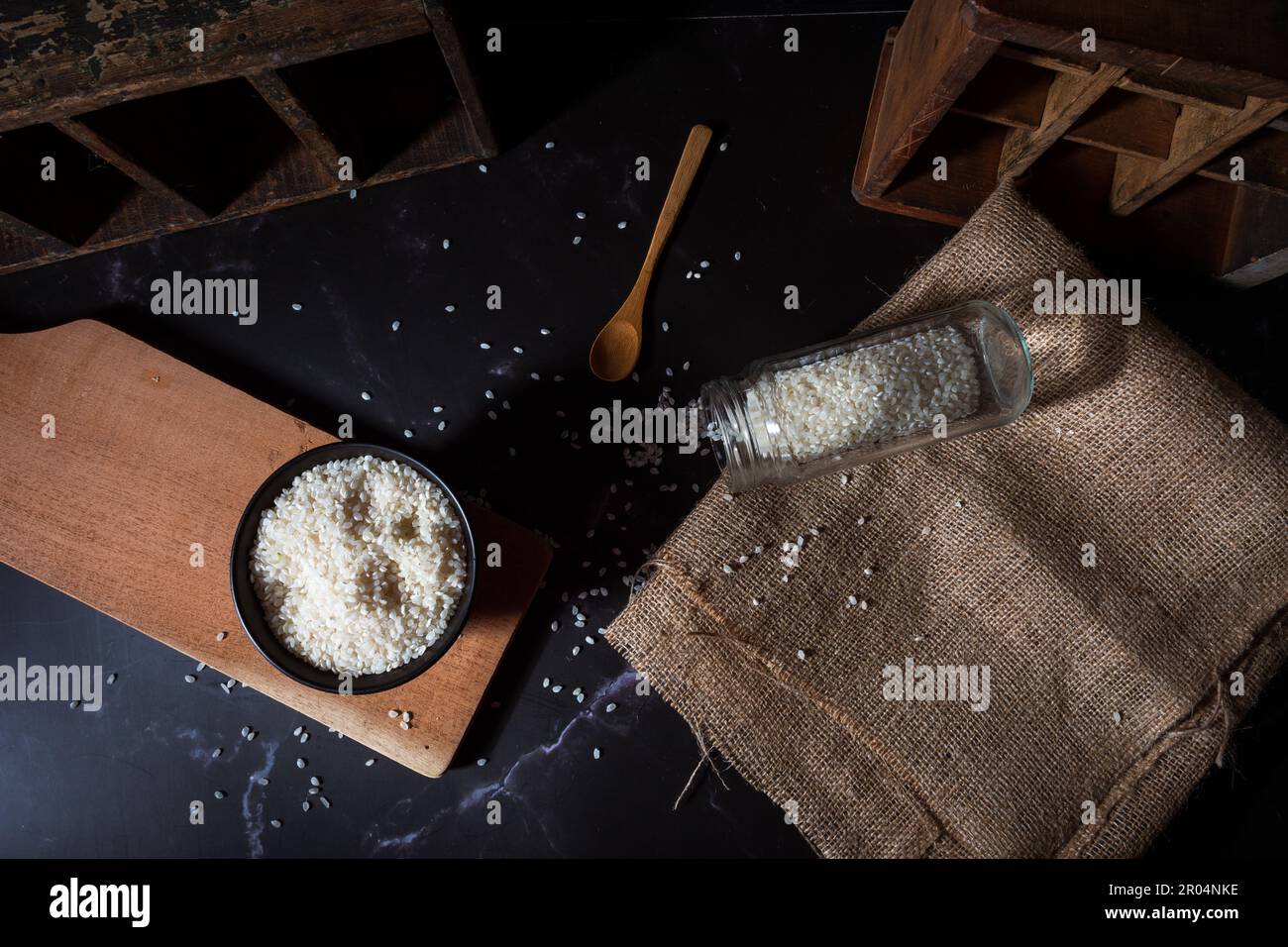 Upside down jar, wooden spoon and black bowl with raw white yamani rice ...