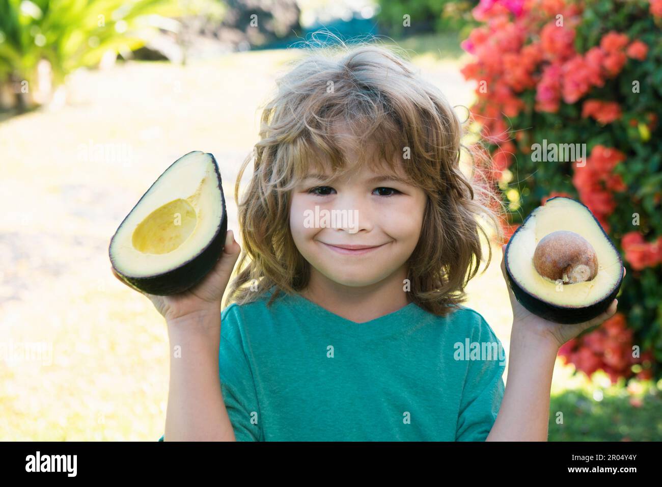 Close up face of kid with half an avocado in her hand, next to her lies ...