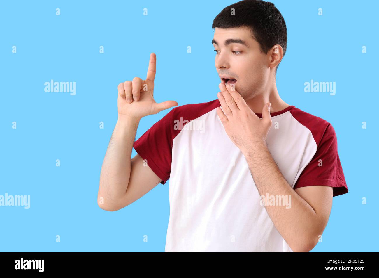 Shocked young man showing loser gesture on blue background Stock Photo ...