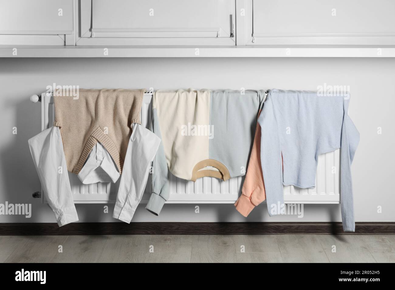 Clean clothes hanging on white radiator in room Stock Photo - Alamy