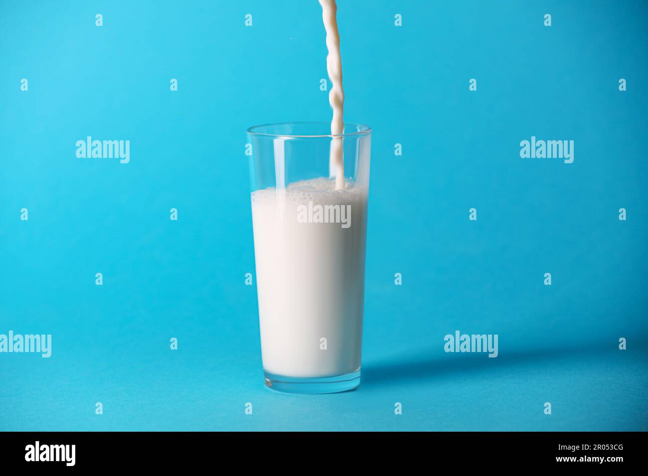 Pouring fresh milk into glass on light blue background Stock Photo - Alamy