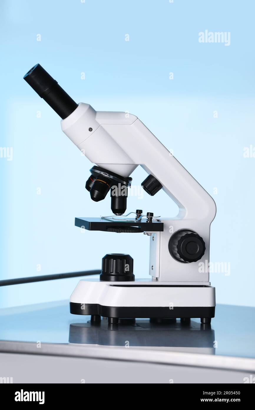 Modern microscope on metal table against light blue background Stock ...