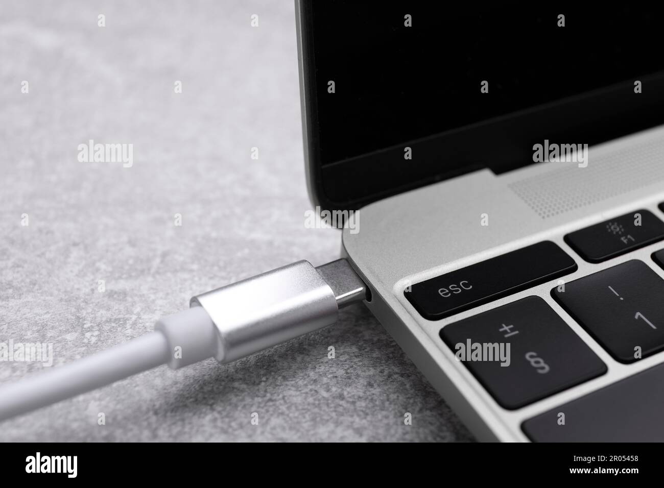 USB cable with type C connector plugged into laptop port on grey table ...
