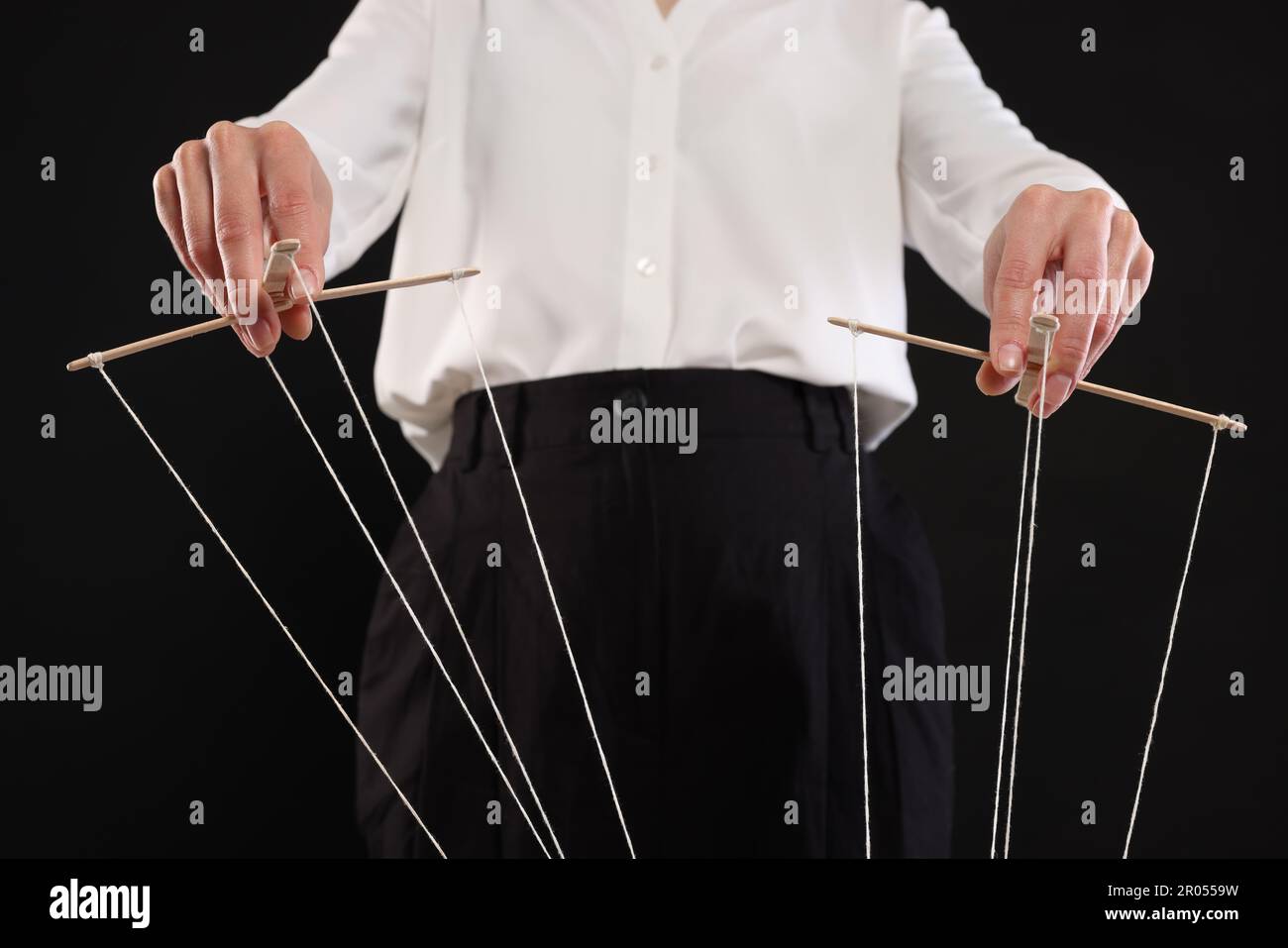 Woman in formal outfit pulling strings of puppet on black background ...