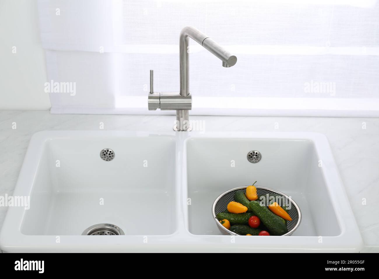 Modern sink with water tap and fresh vegetables near window in kitchen ...