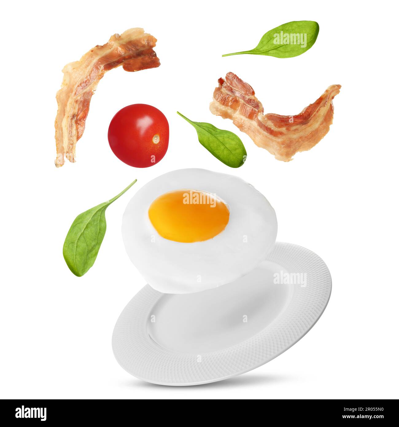 Tasty fried chicken egg, bacon, tomato and basil leaves falling into ...