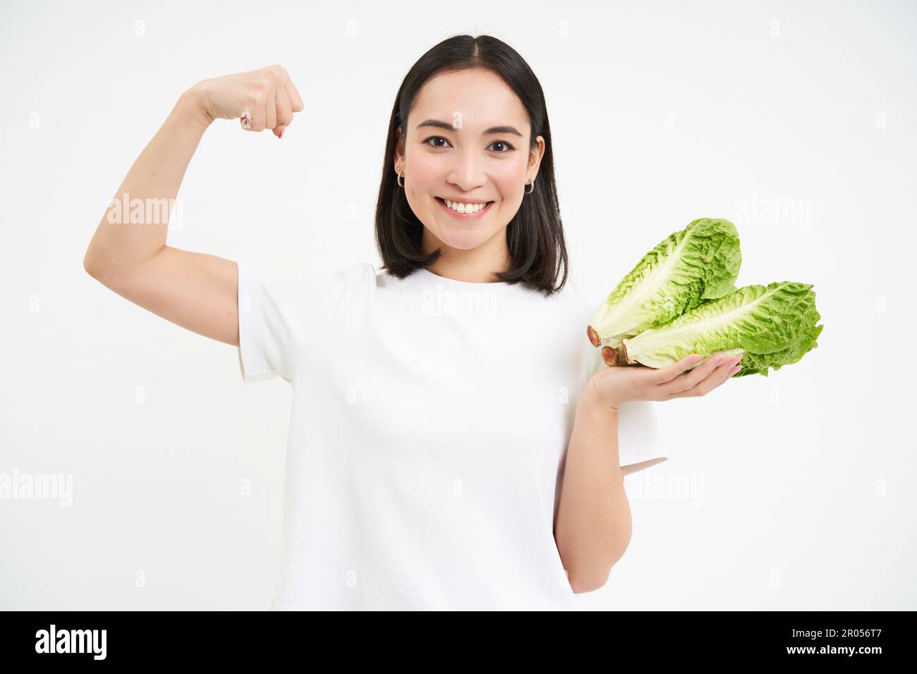 Strong asian woman shows fresh vegetables, lettuce and her muscles ...