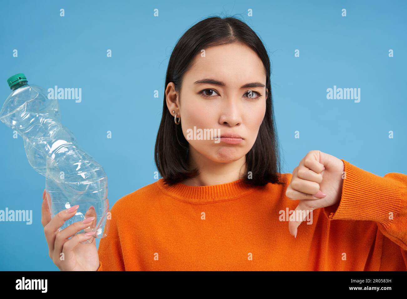 Portrait of asian woman shows thumbs down and plastic bottke ...