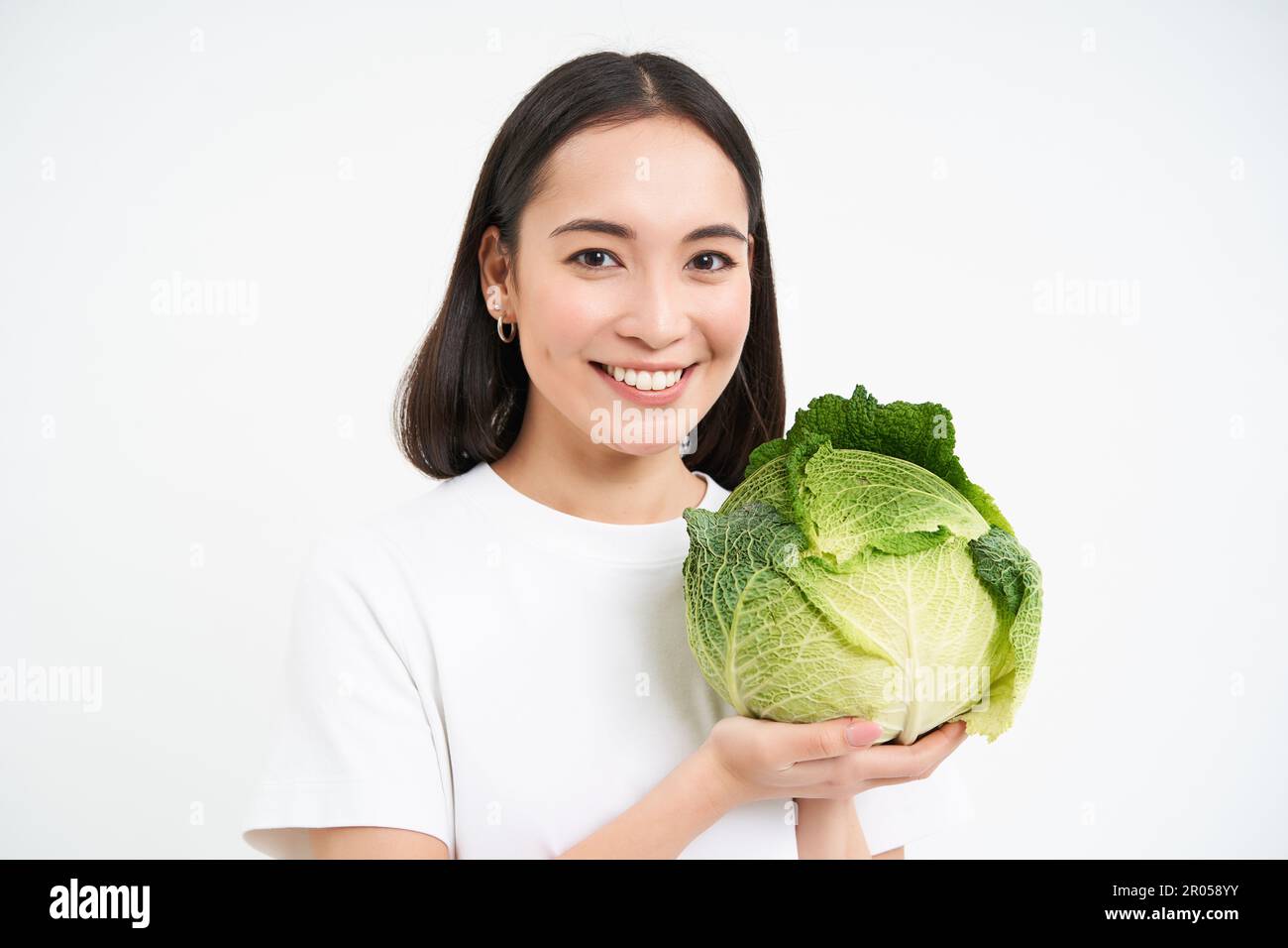 Close up portrait of young asian woman, smiling and proudly showing her self grown vegetable ...