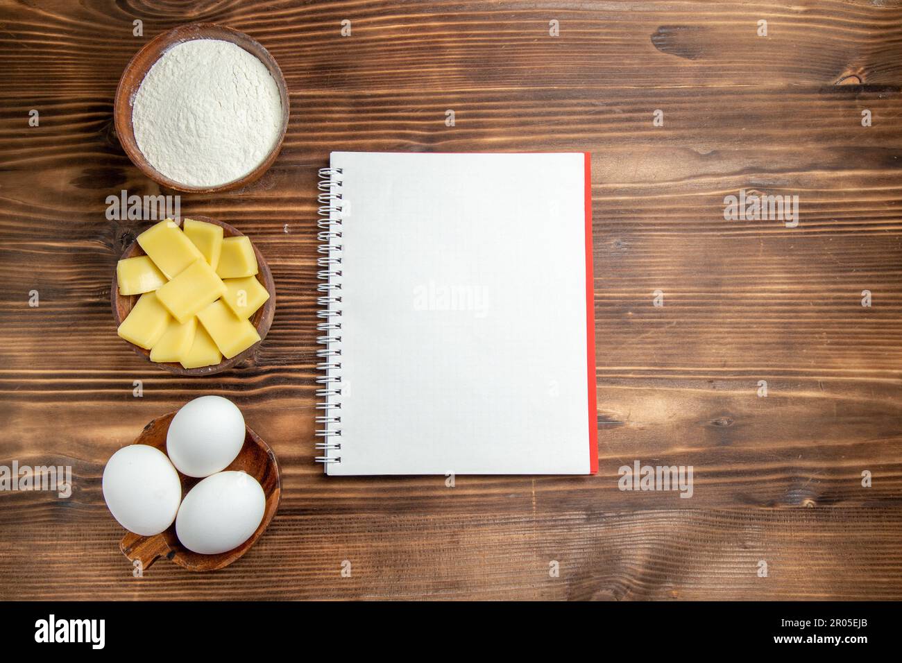 top view whole raw eggs with flour notepad and cheese on brown table ...