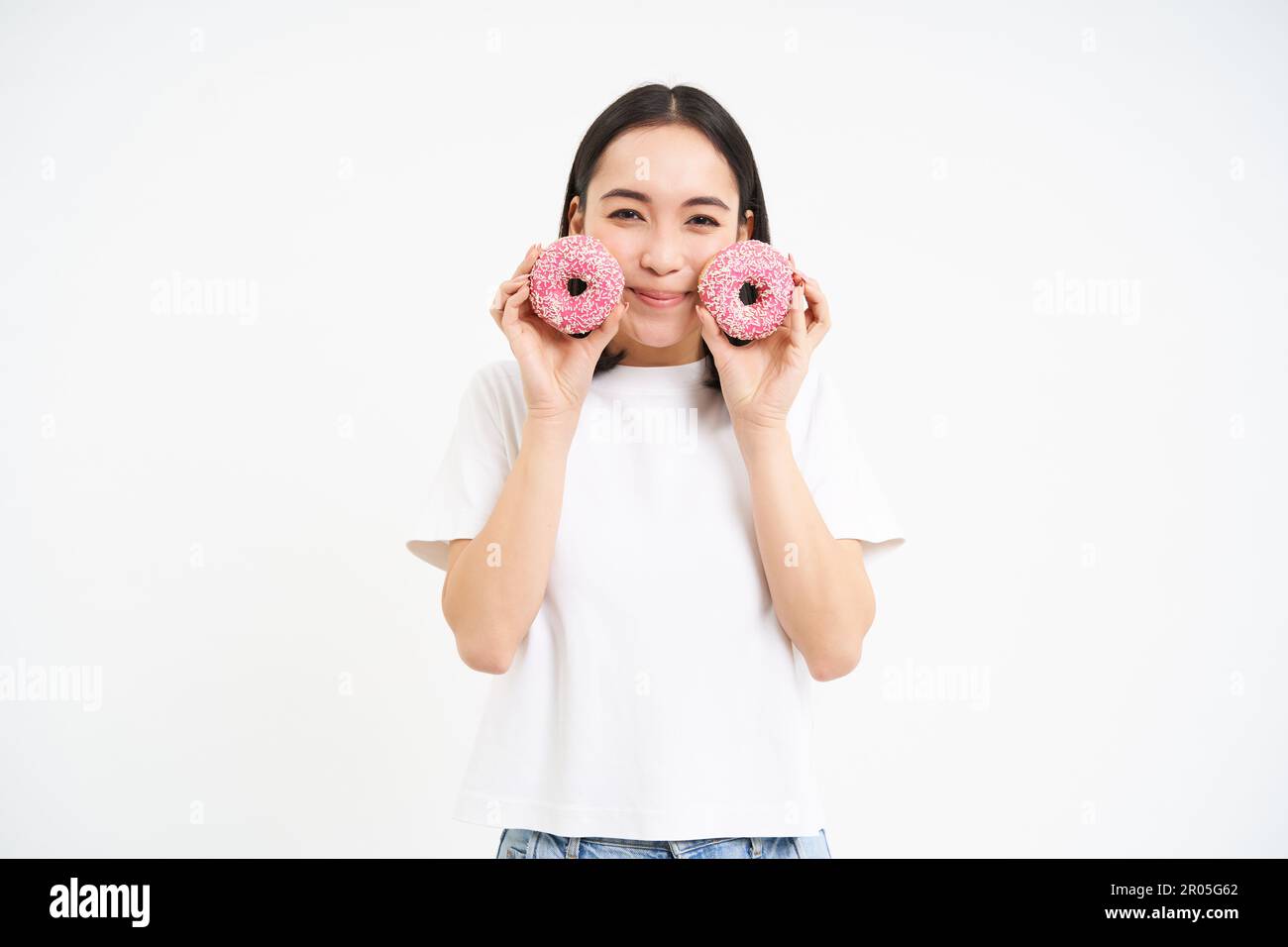 Beautiful young woman eating delicious glazed dougnuts, holding two ...