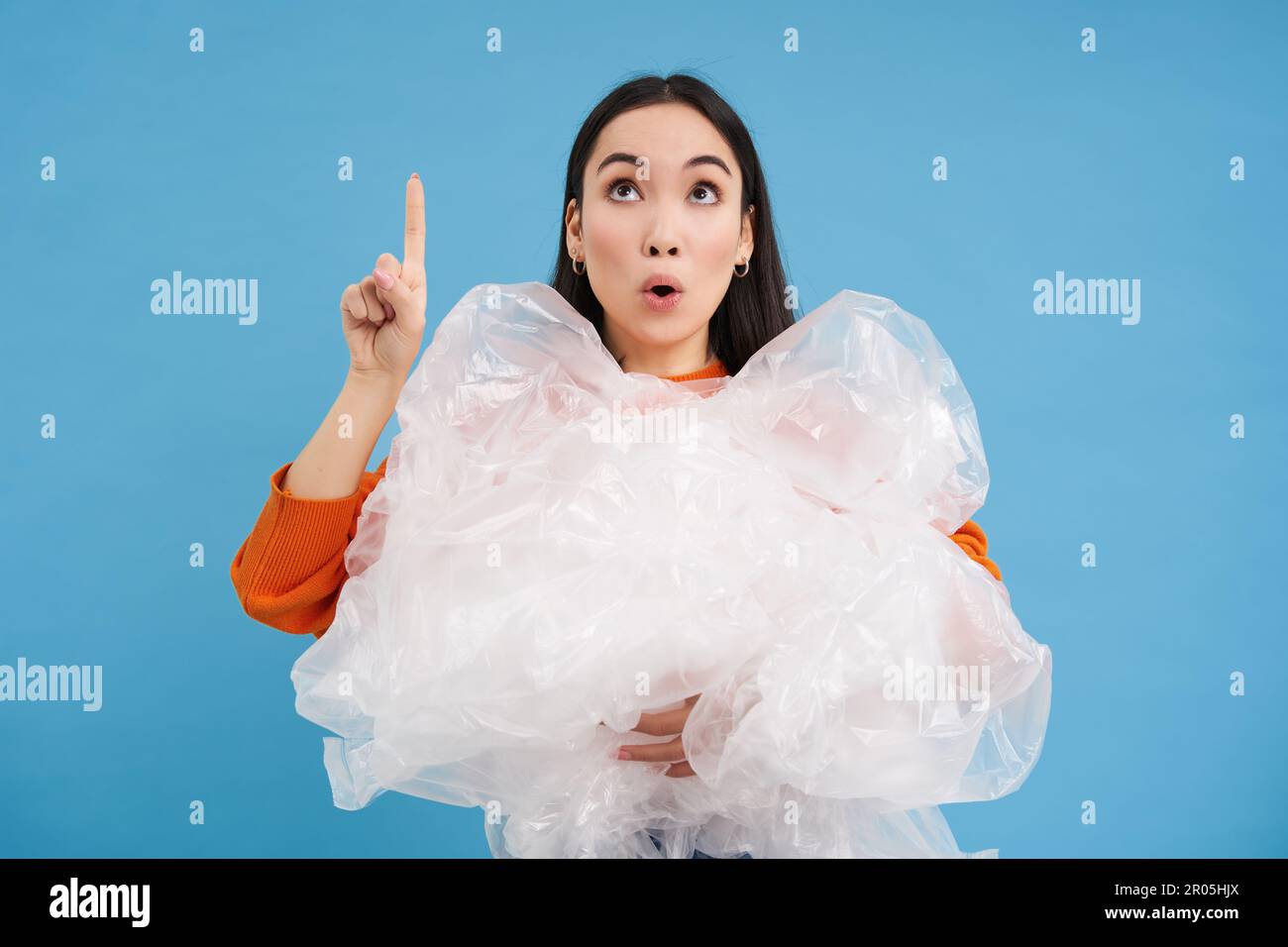 Surprised korean woman with plastic waste, points finger up and looks ...