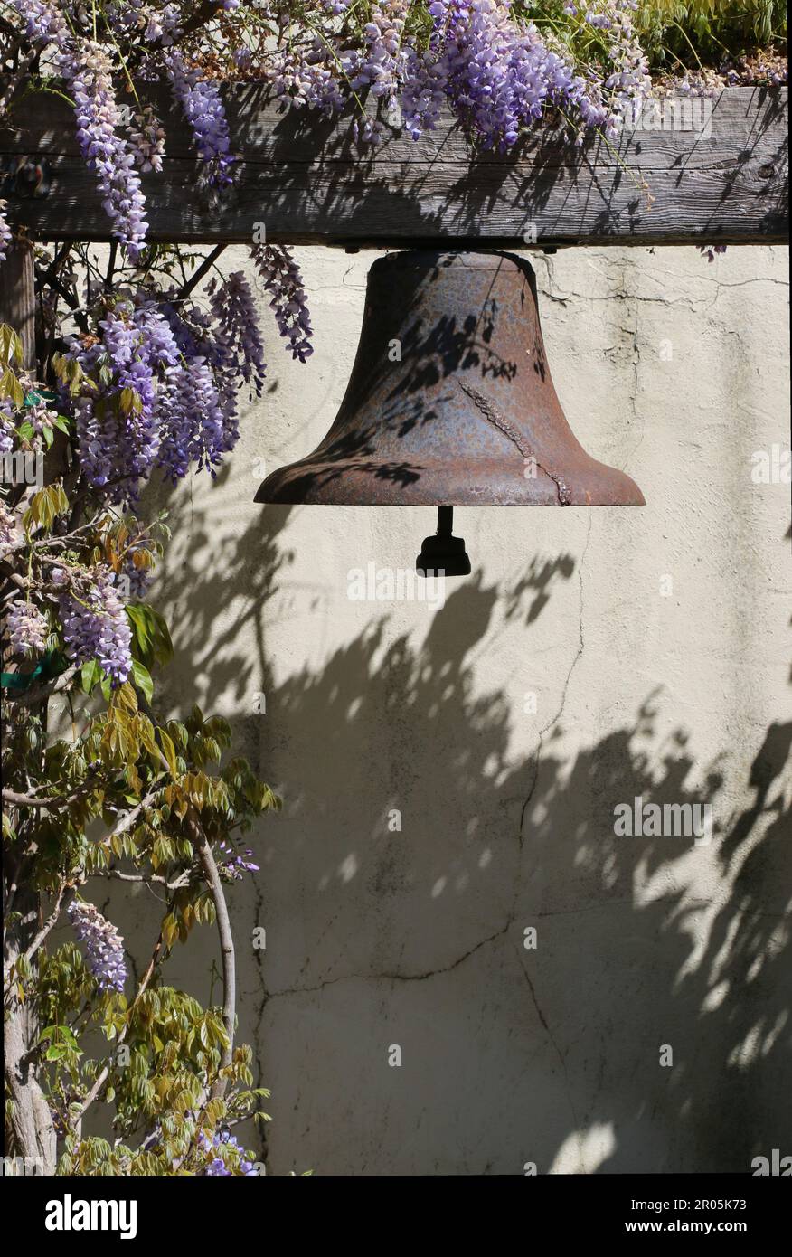 Old, weathered bell suspended from a weathered wood beam with trailing ...