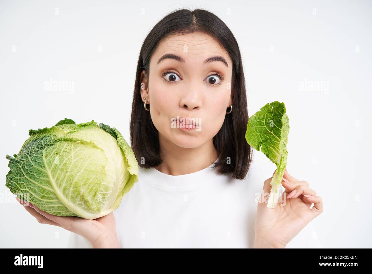 Close up of cute korean woman, eating cabbage, on diet, holding lettuce, isolated on white ...