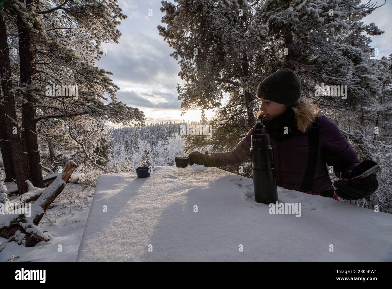 Woman sitting in snowy outdoor environment drinking tea out of thermos ...