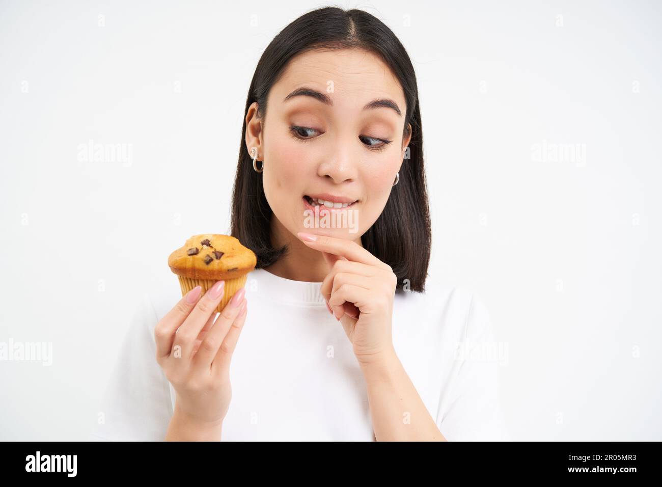 Image of pensive korean woman, looks at cupcake with thoughtful face ...
