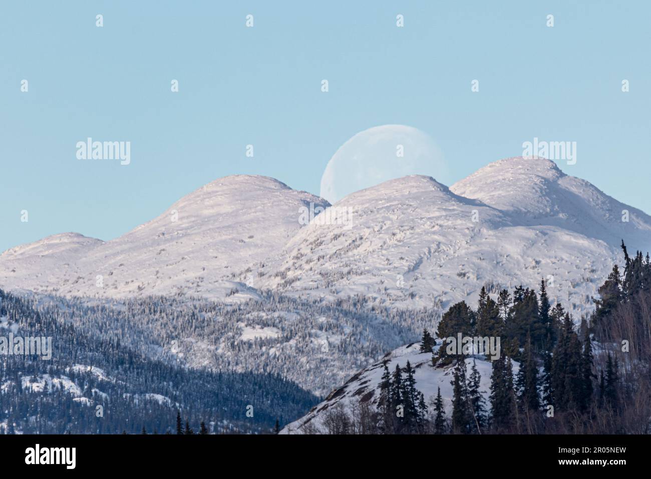 Moon setting over beautiful snow capped mountains in northern Canada ...