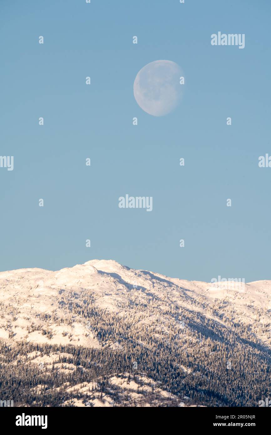 Moon setting over beautiful snow capped mountains in northern Canada ...