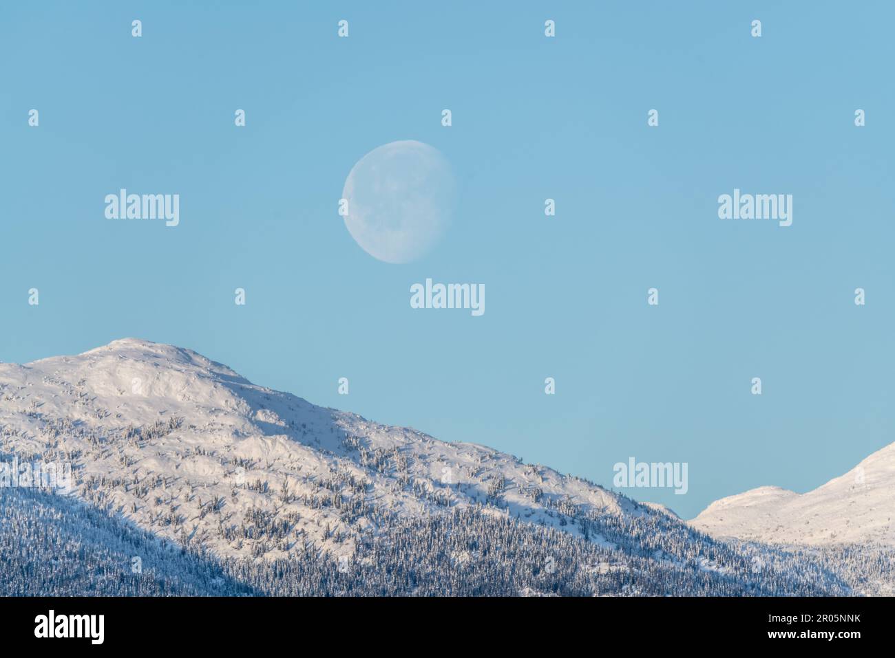 Moon setting over beautiful snow capped mountains in northern Canada ...