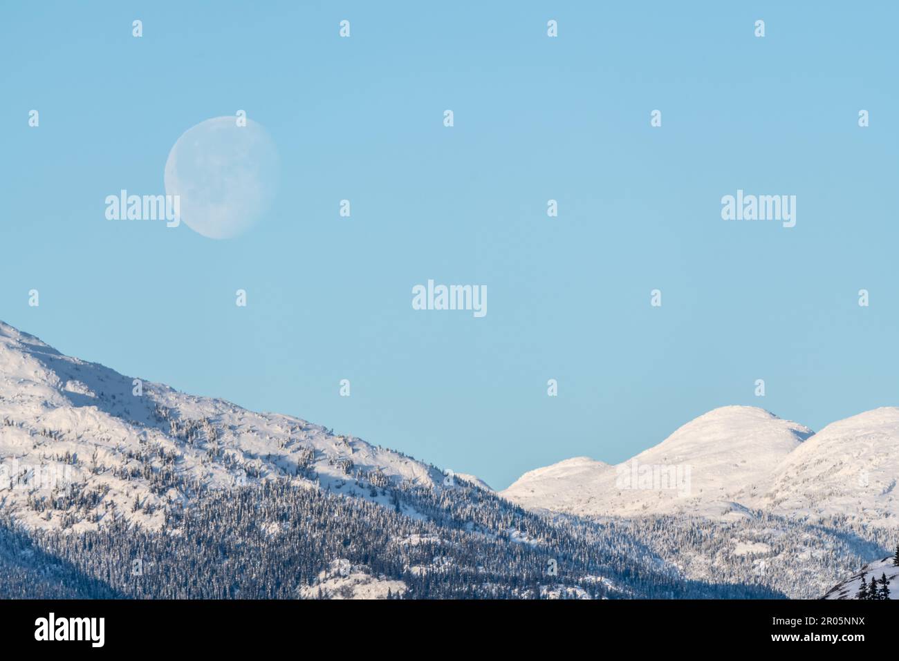 Moon setting over beautiful snow capped mountains in northern Canada ...