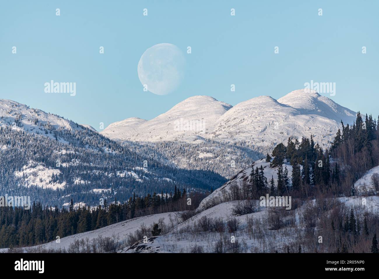 Moon setting over beautiful snow capped mountains in northern Canada ...