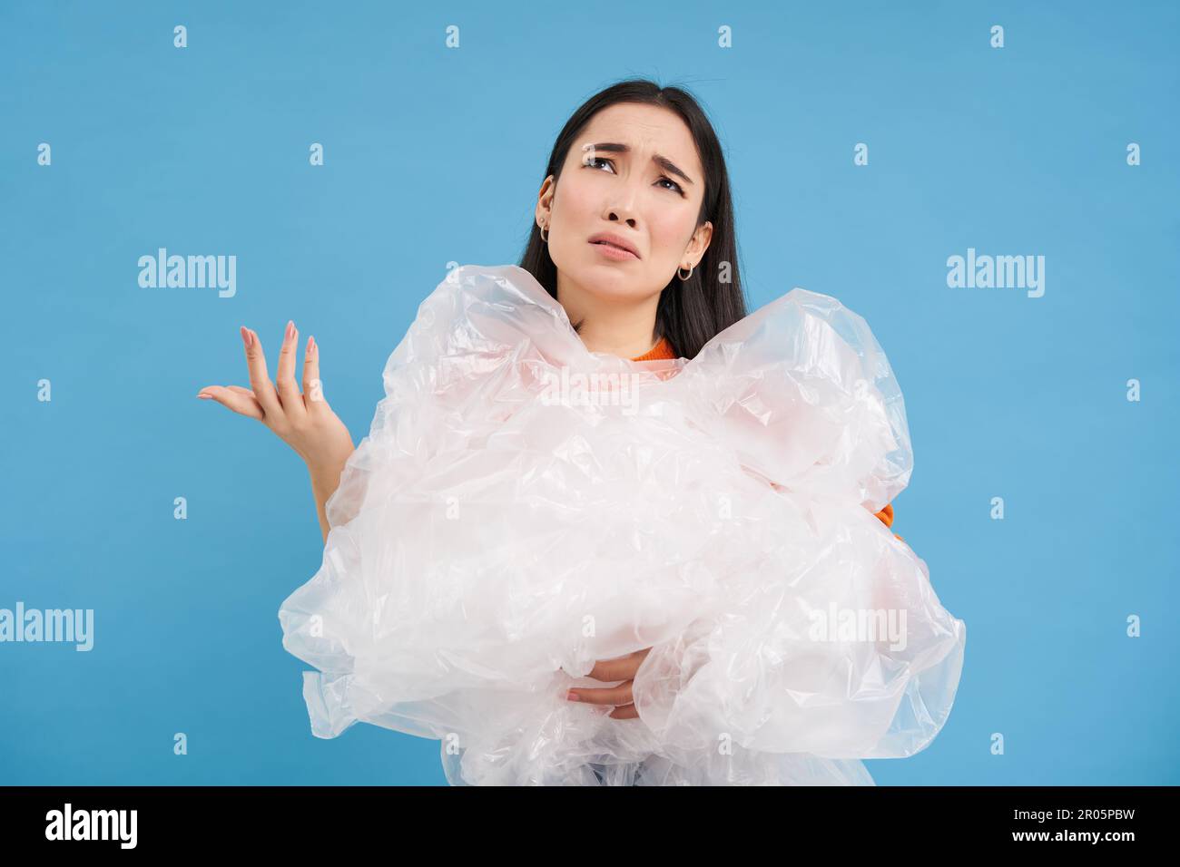 Disappointed asian woman with plastic garbage in hands, shrugging with ...