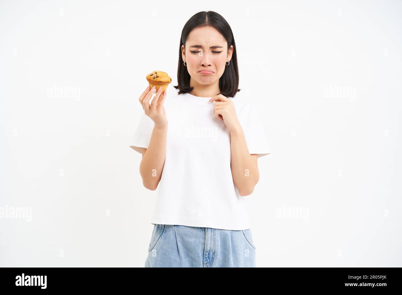 Portrait of unhappy korean woman looks at cupcake with sad face, girl ...