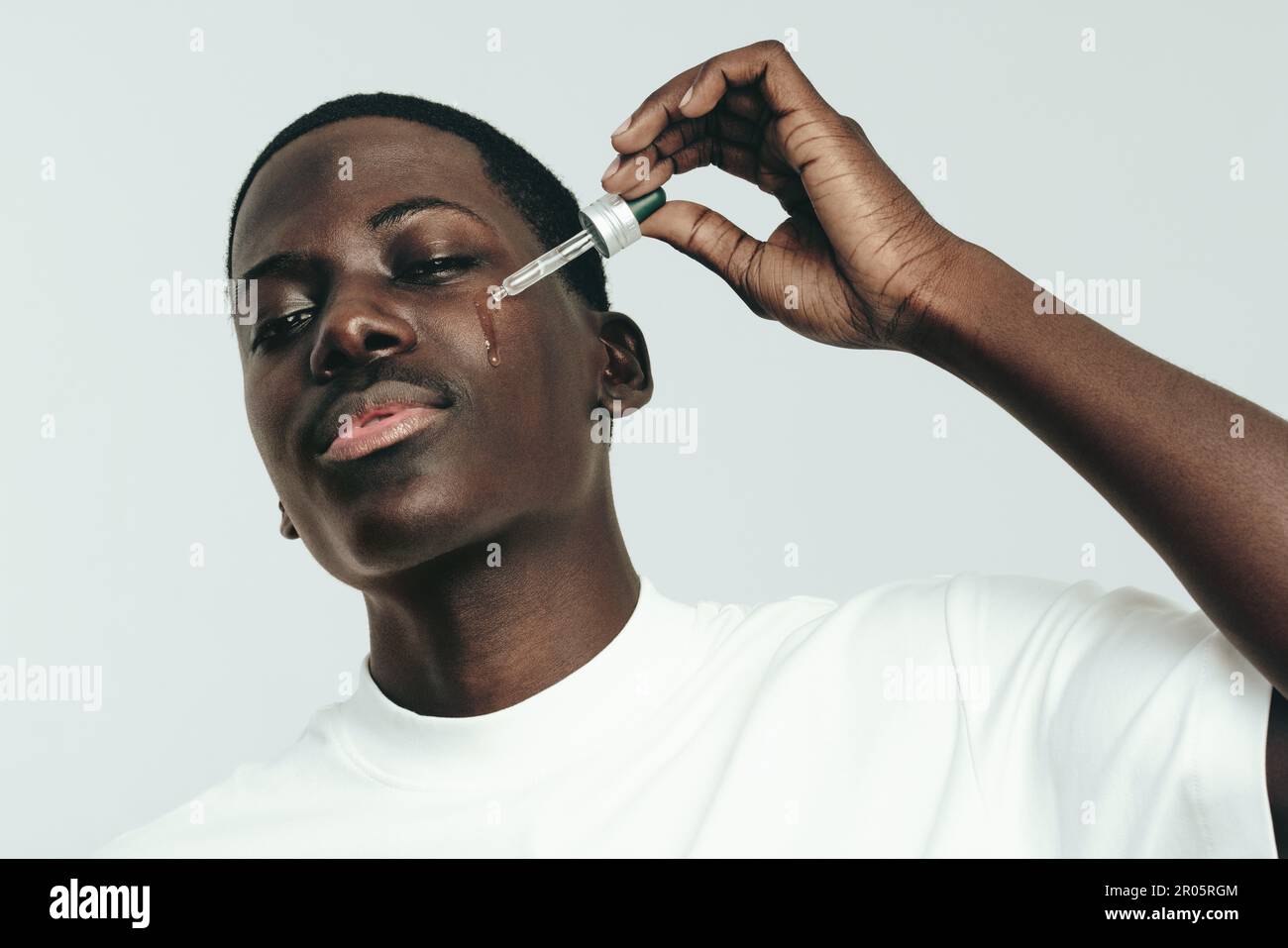 Young black man applying beauty serum on his face. Confident young man ...