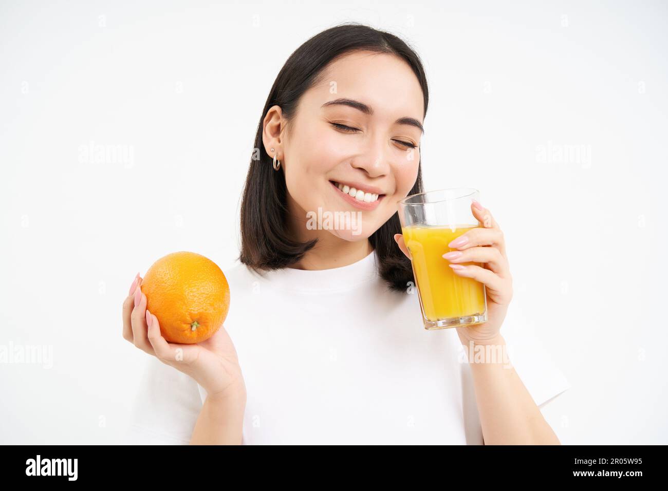 Woman drinking fresh juice, holding orange fruit and smiling, feeling ...