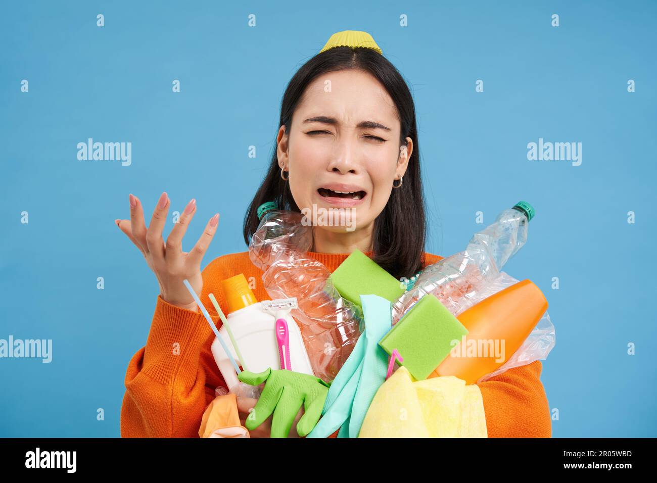 Frustrated asian woman crying, holding loads of empty plastic bottles ...