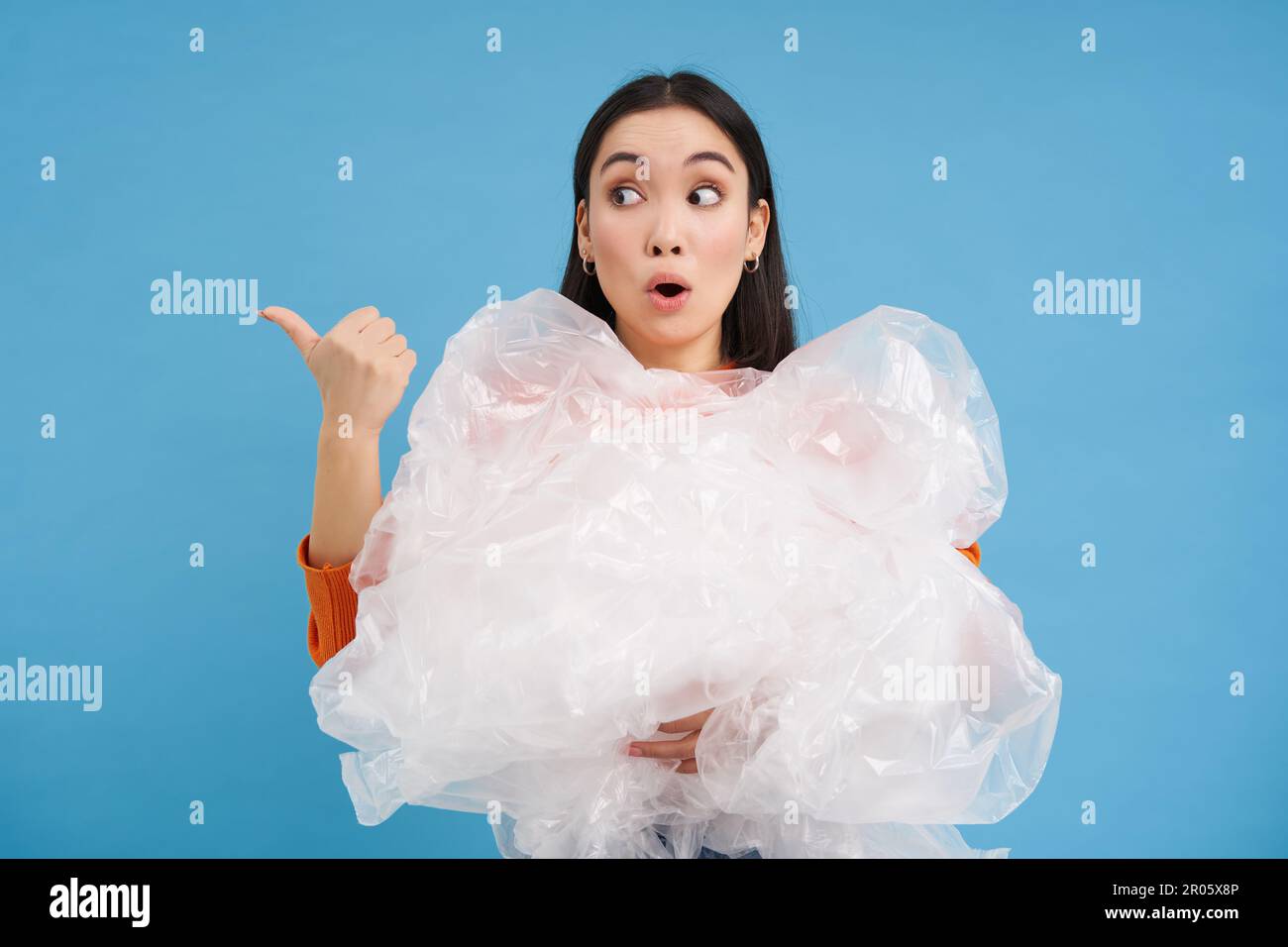 Woman with surprised face, holding plastic recycling waste and pointing ...