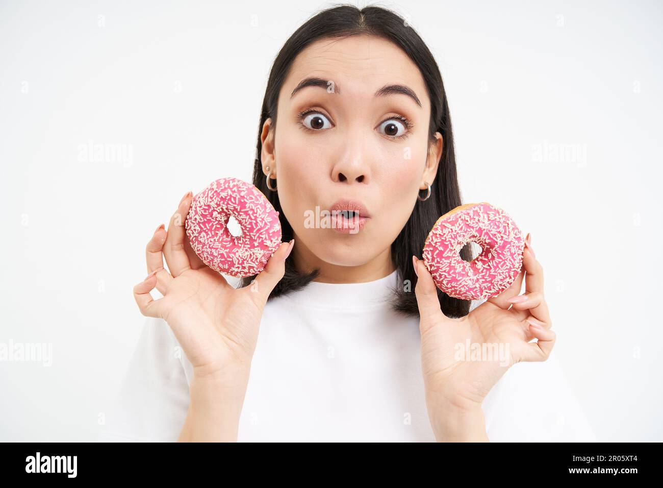 Close up of girl with amazed face, shows two glazed doughnuts, tempted ...