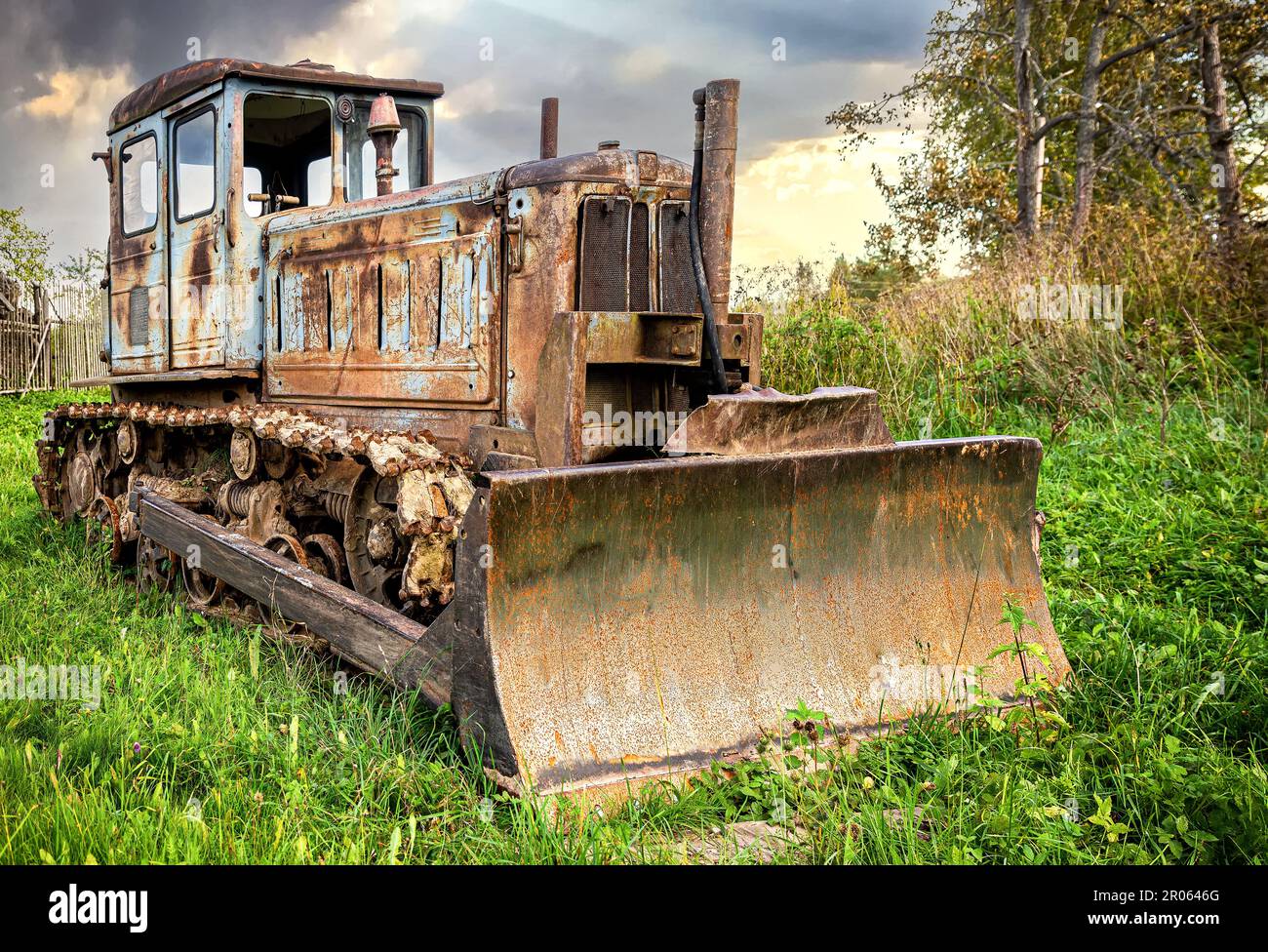 Old crawler rusty tractor on the green grass at the summer village ...
