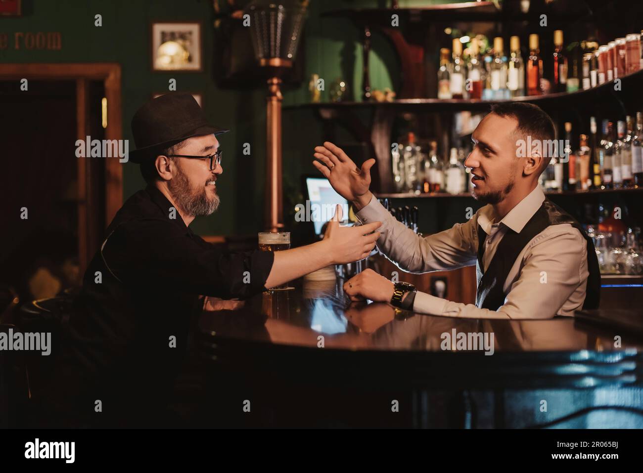 man has fun chatting with a bartender at bar counter with a glass of ...