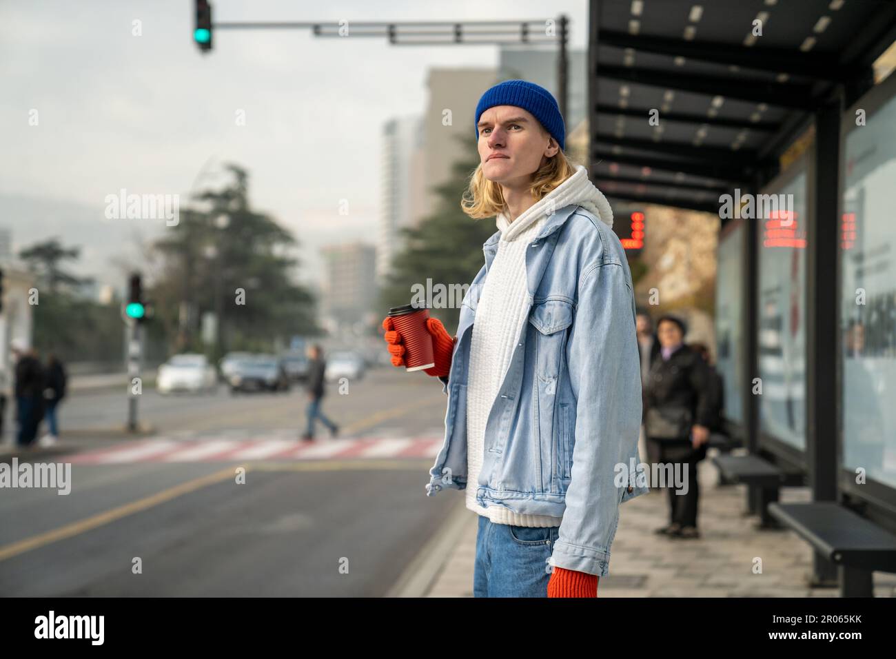 Young man with take away coffee cup waiting for bus at public transport ...