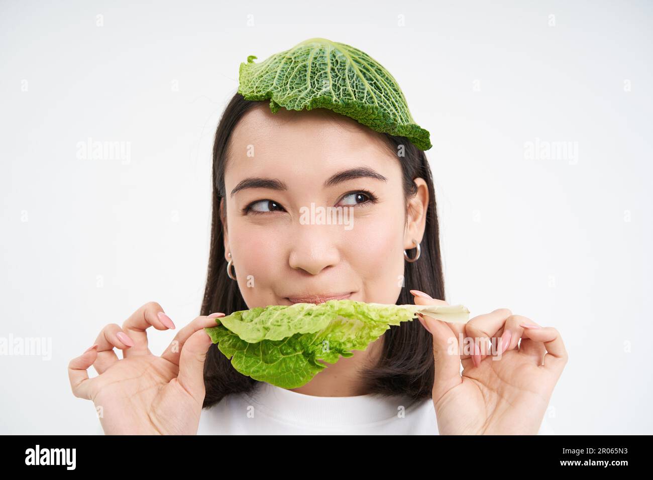 Portrait of asian girl with leaf on head, eats cabbage and smiles ...