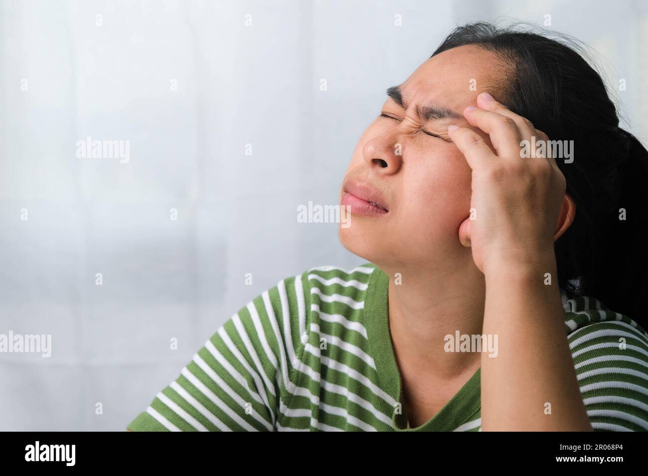 Young woman having headache against white curtain background in room ...