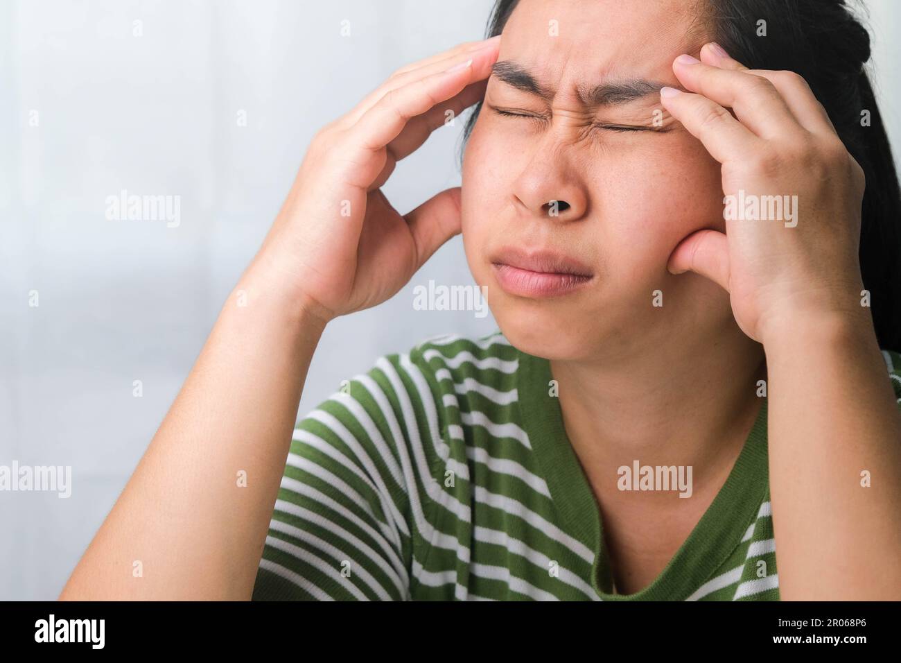 Young woman having headache against white curtain background in room ...