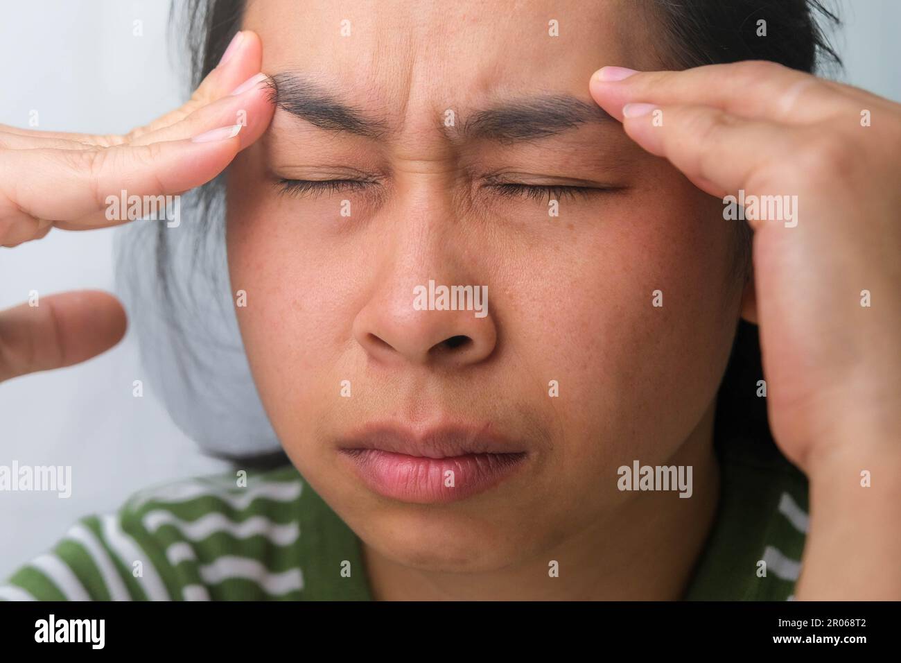 Young woman having headache against white curtain background in room ...