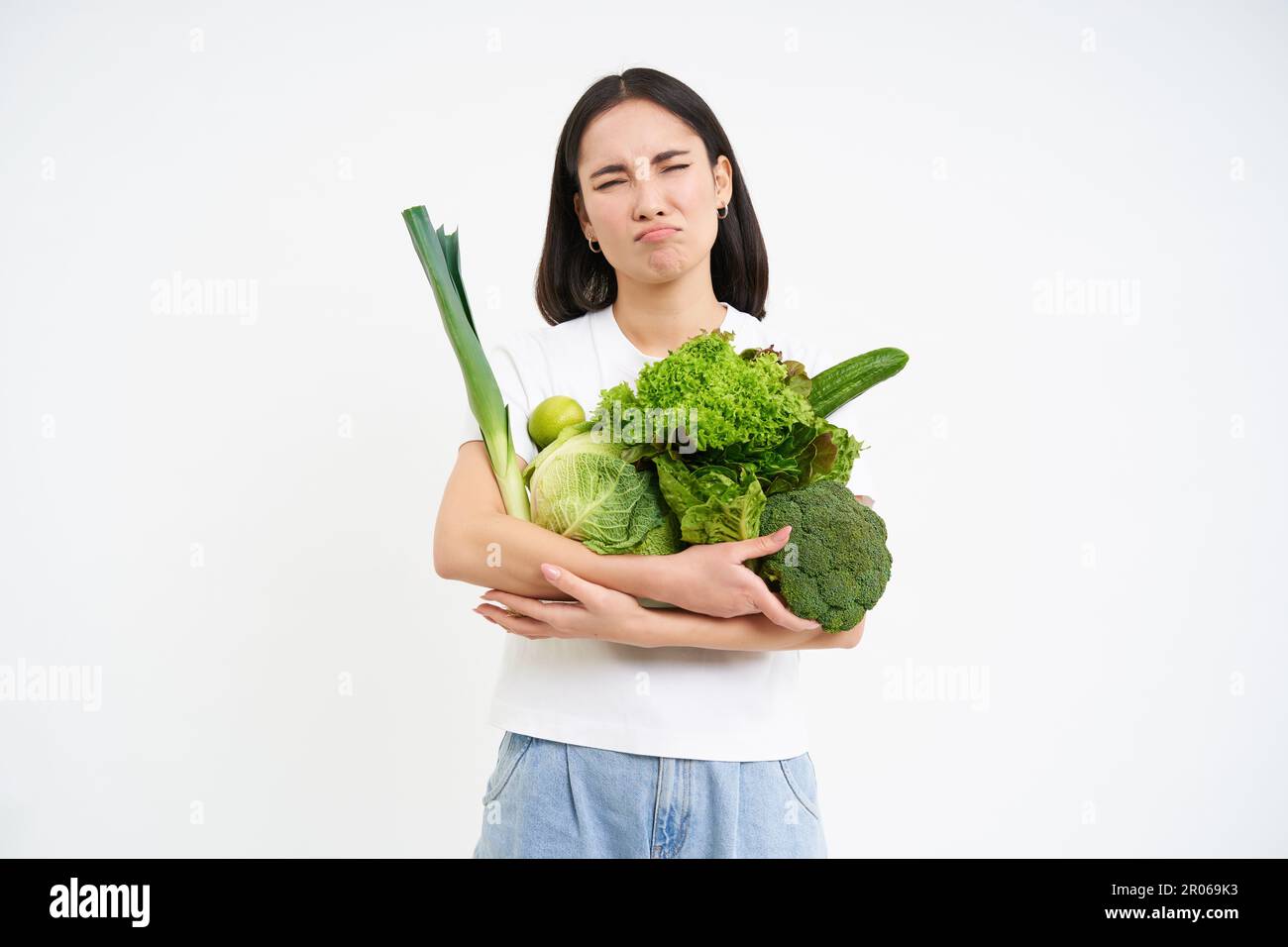 Woman with disgusted face, holding vegetables, green organic food ...
