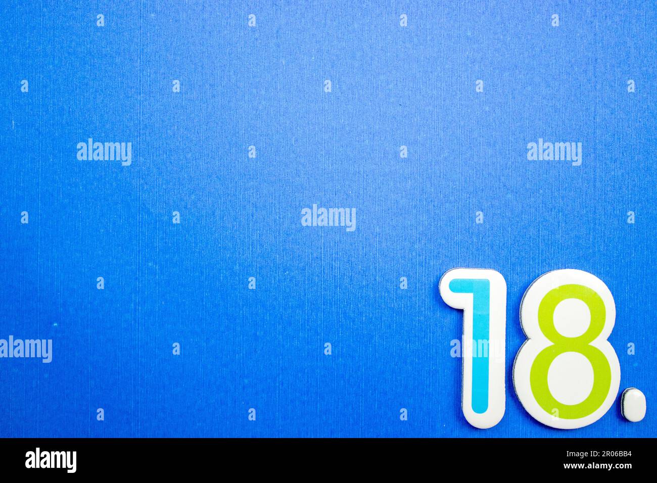 The number 18 in light blue and green color, photographed from above, placed on the edge of a ...
