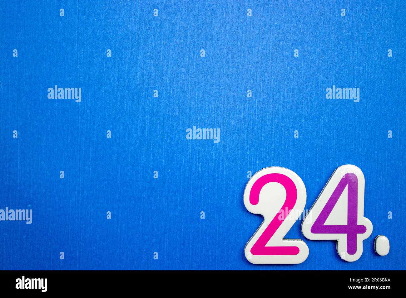 The number 24, placed on the edge of a blue background, photographed from above, colored red and ...